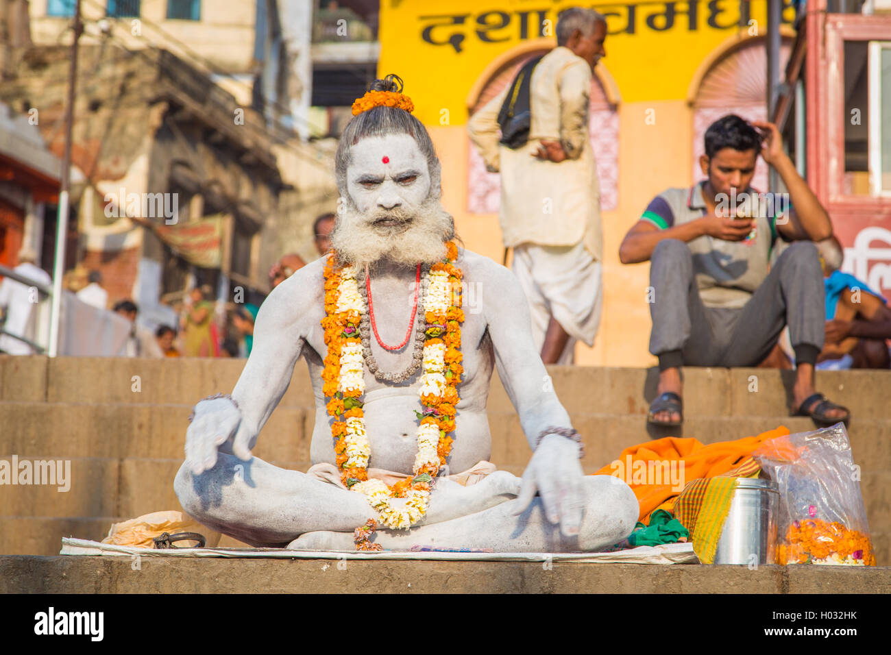 VARANASI, INDIA - 23 FEBRUARY 2015: Sadhu sits on ghat with legs ...