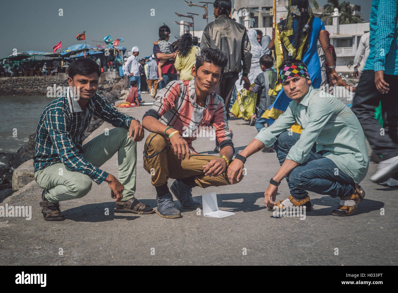 MUMBAI, INDIA - 09 JANUARY 2015: Three Indian boys crouch next to sea ...