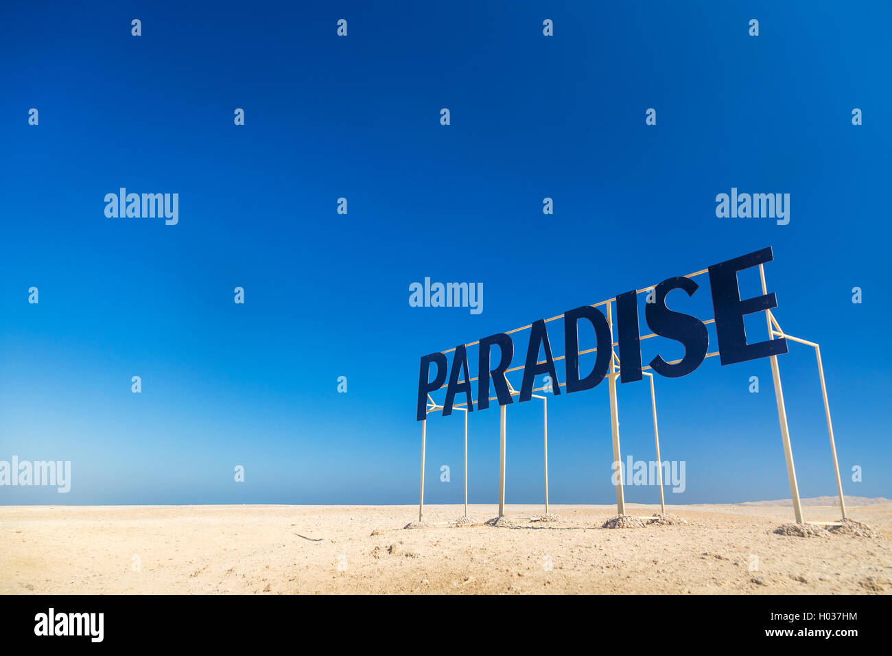 Paradise sign on sand against clear blue sky Stock Photo - Alamy