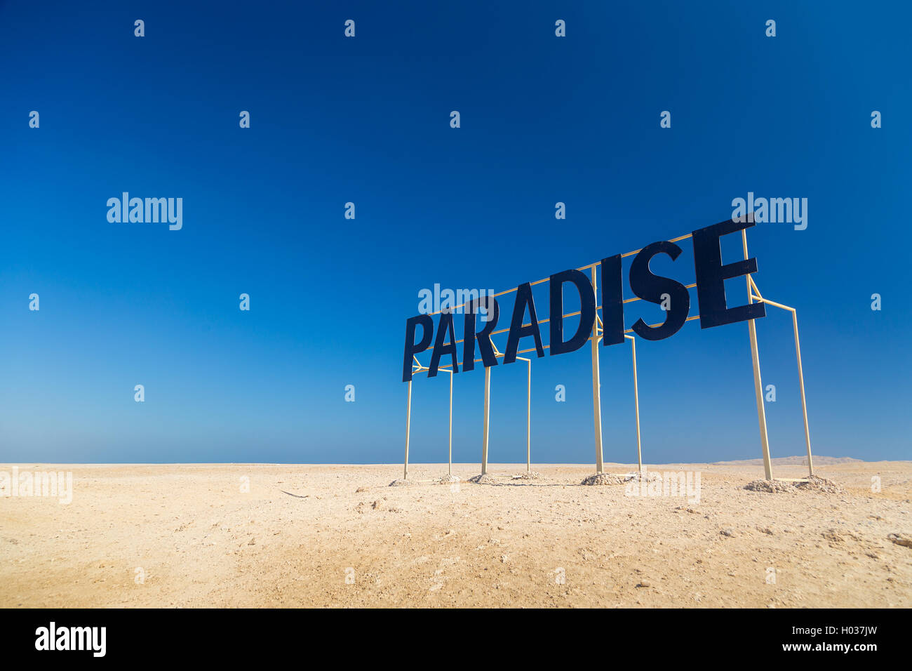 Paradise sign on sand against clear blue sky Stock Photo - Alamy