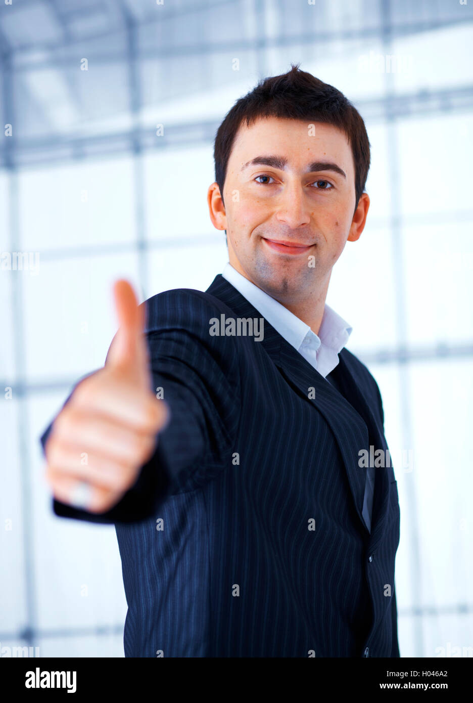 Happy handsome business man giving you a thumbs up sign against windows ...