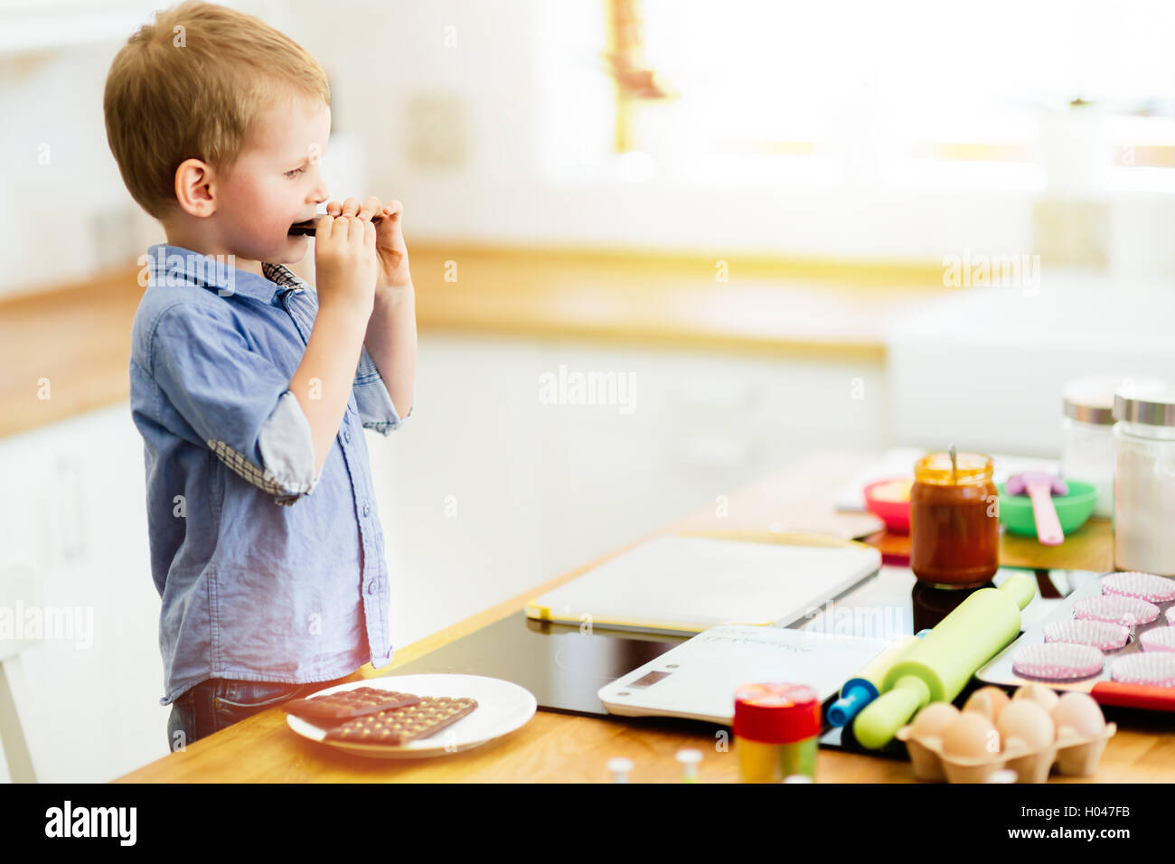 Cute child preparing food in kitchen by standing on chair Stock Photo ...