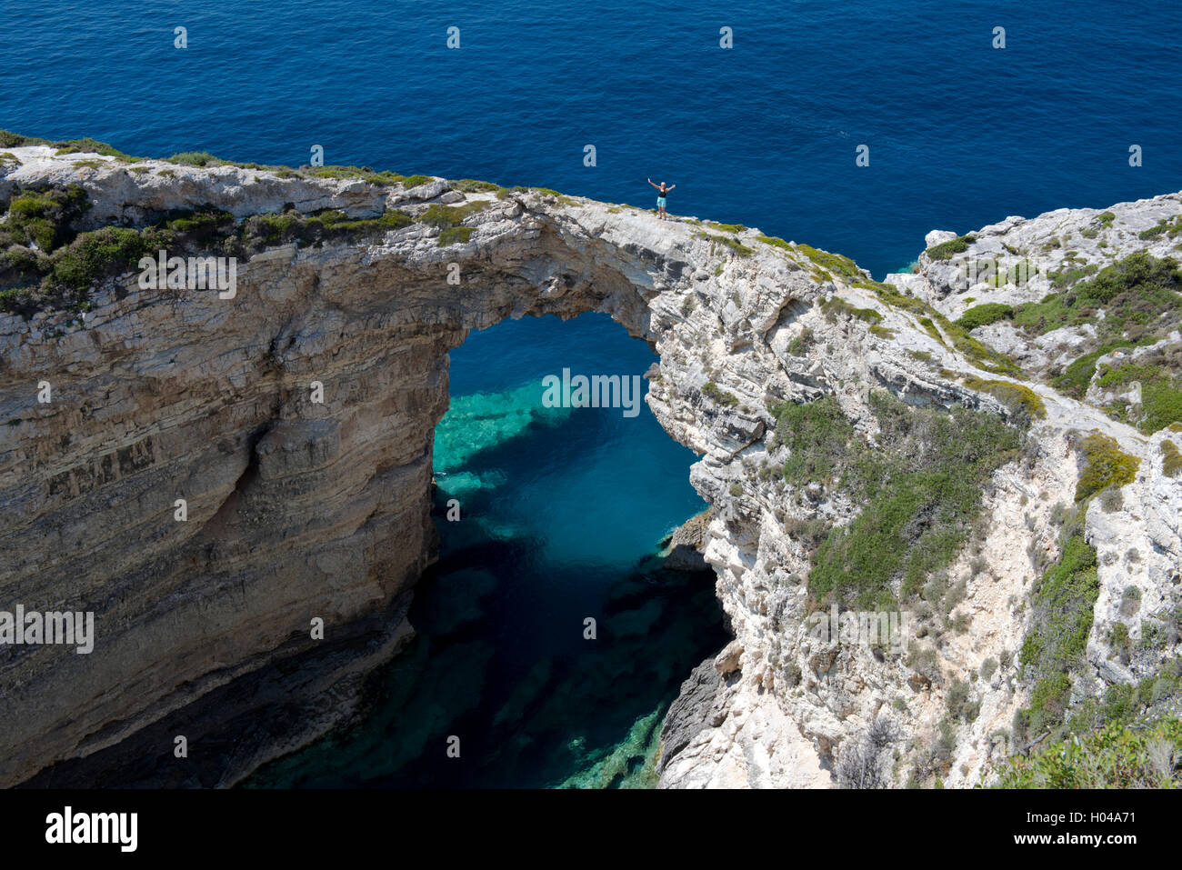 A tourist waving from the top of the Trypitos Arch, a limestone arch ...