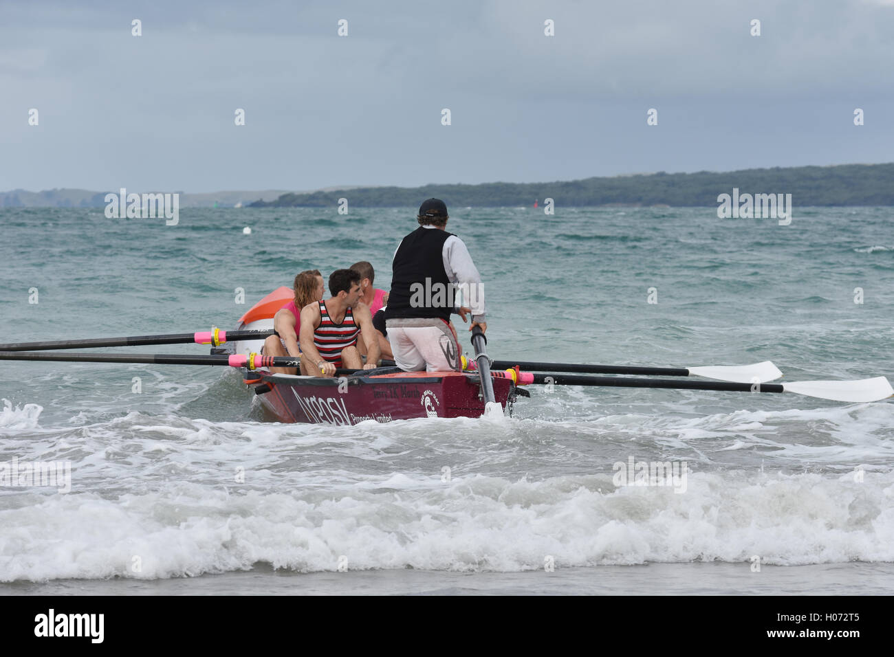 Rowing boat being launched from sandy beach through oceanic surf waves ...