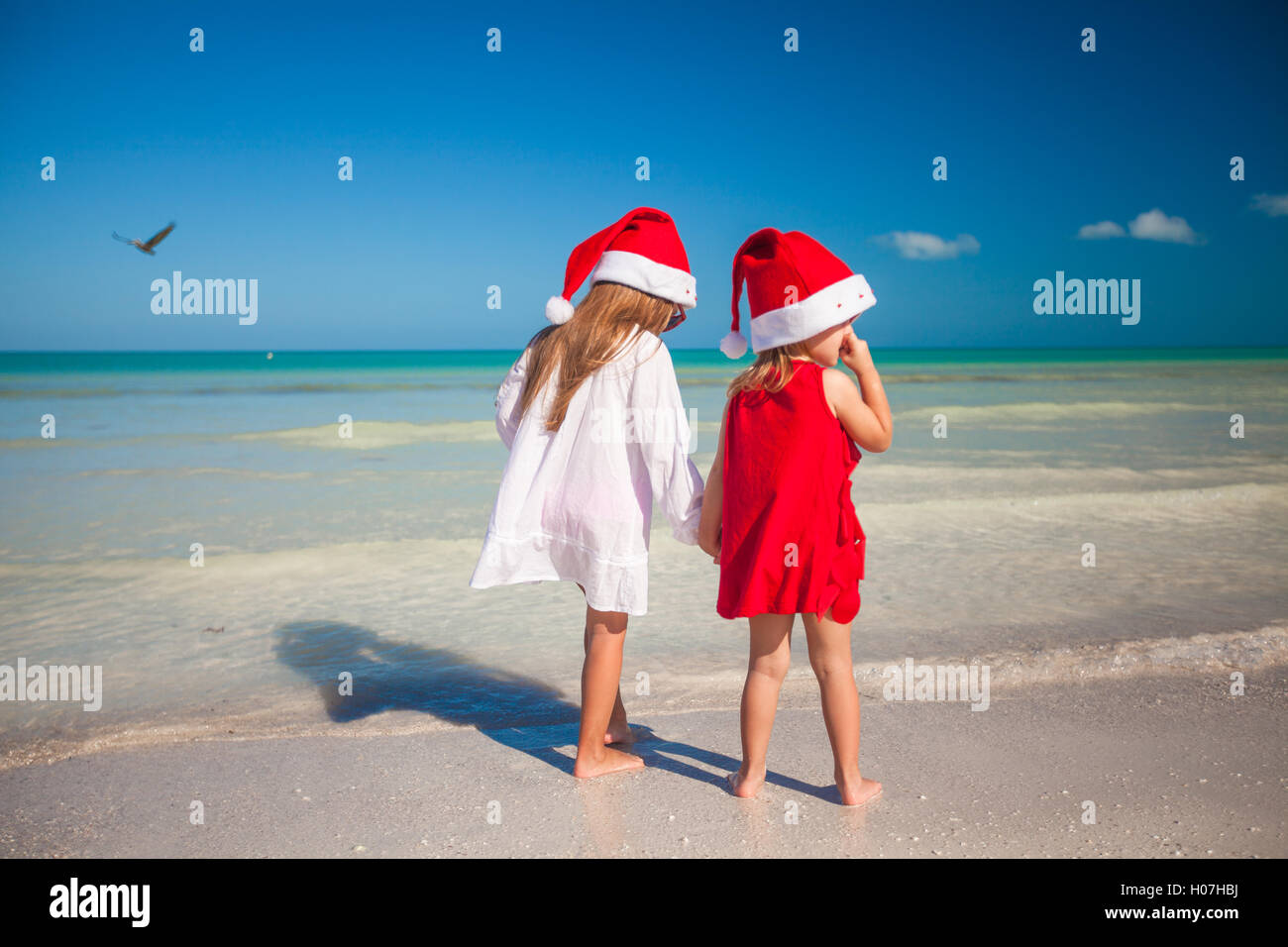 Rear view of Little cute girls in Christmas hats on the exotic beach ...