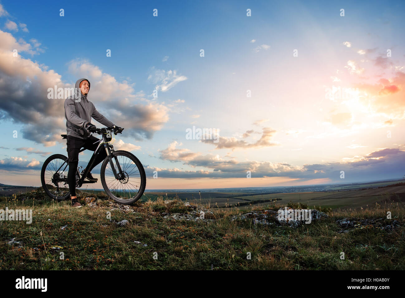 Young man cycling on a rural road through green spring meadow during ...