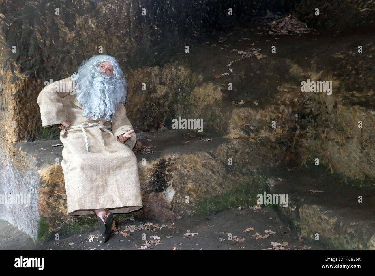 Thinking hermit sitting at the rocky seat in cave. The bearded ...