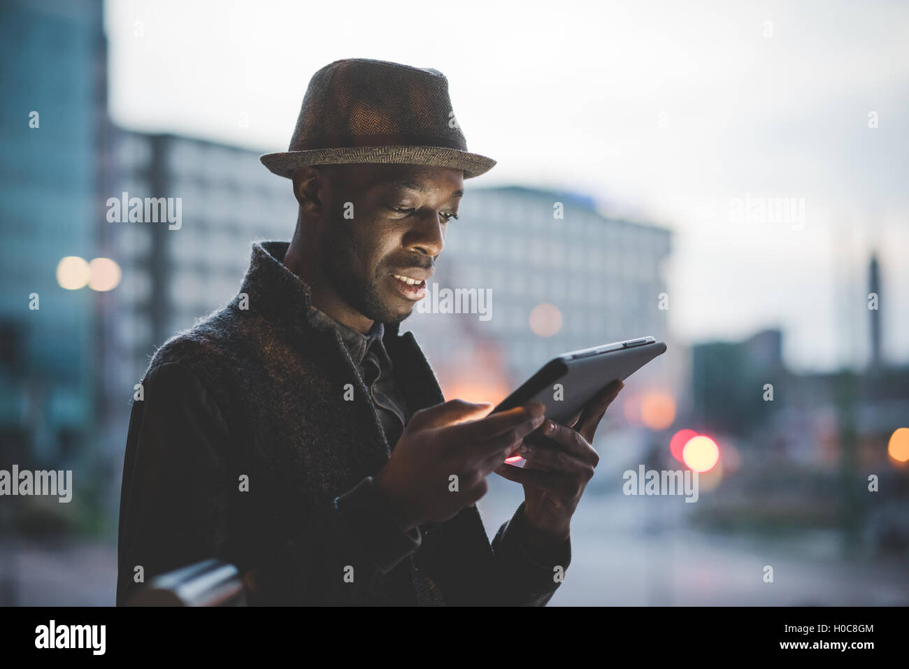 Portrait of young handsome afro black man using a tablet, looking downward the screen, pensive ...