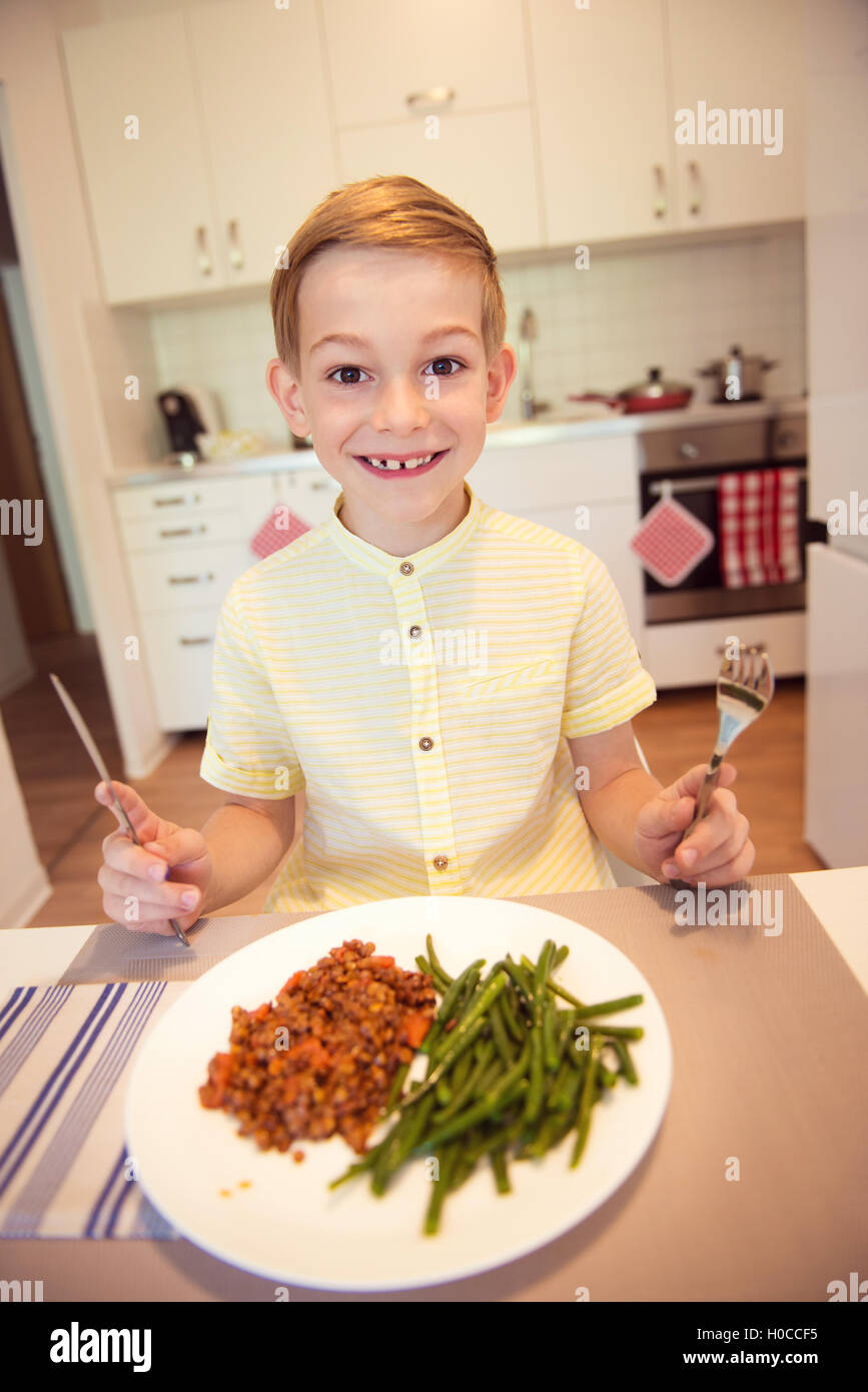 Young diligent happy boy at a table eating healthy meal using cutlery ...
