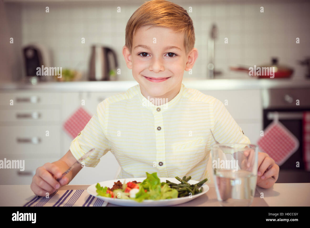 Young diligent boy at a table eating healthy meal using cutlery Stock ...