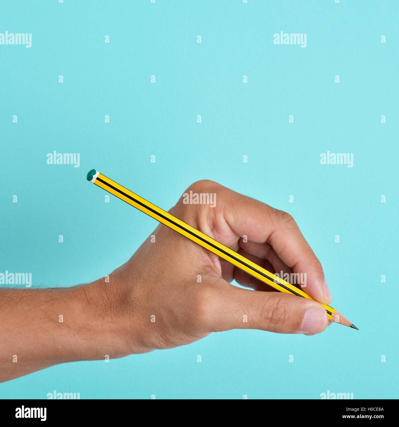 the hand of a left-handed man with a pencil, against a blue background ...