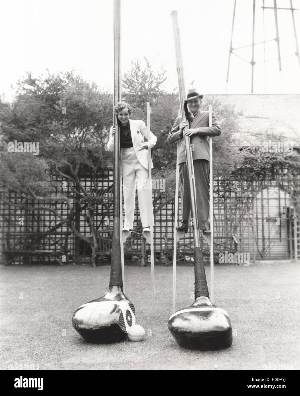 Man and woman on stilts holding giant golf clubs Stock Photo - Alamy