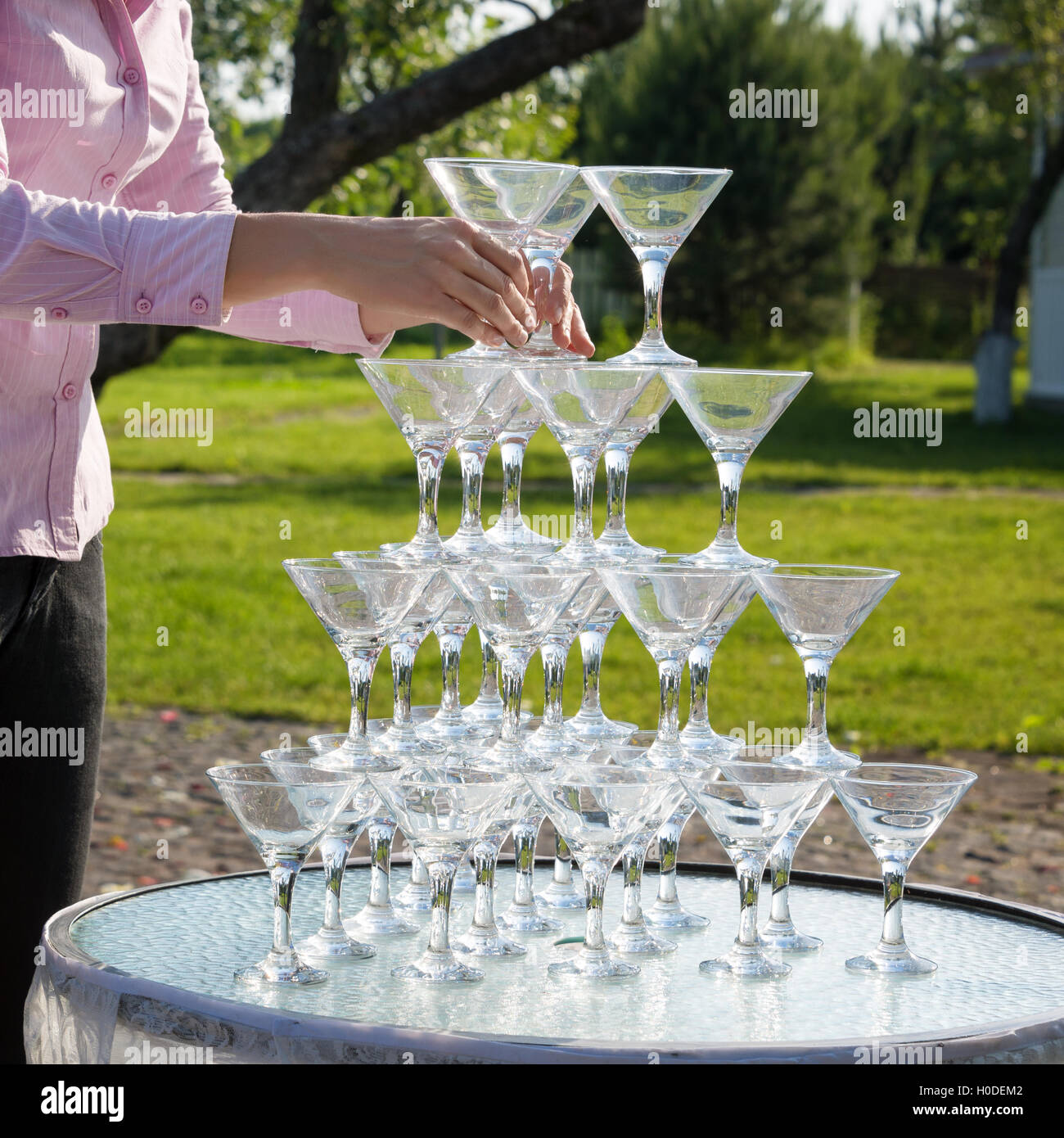 Waiter builds a pyramid of glasses for champagne at outdoor garden in ...