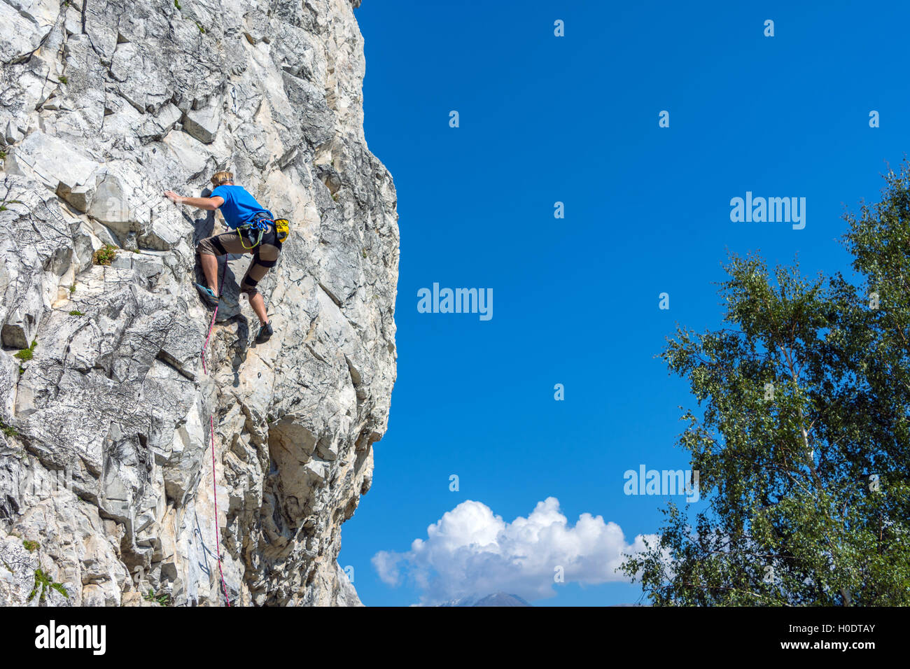 Slim male rock climber in blue on steep rock face, with blue sky ...