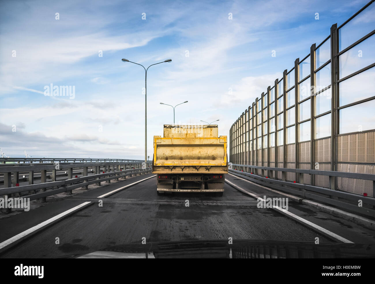 Big yellow industrial tipper truck goes on asphalt road, rear view from ...