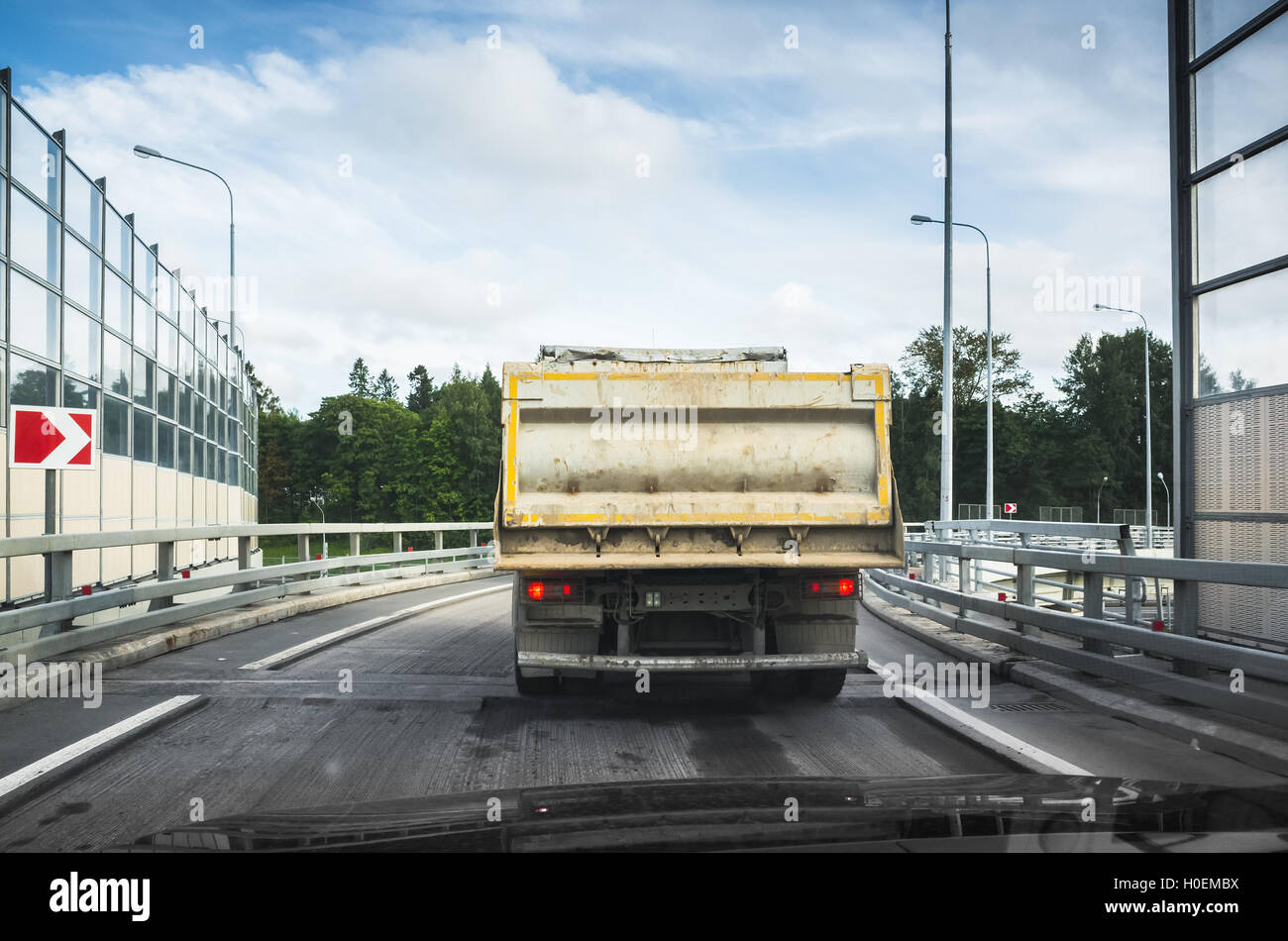 Big industrial tipper truck goes on asphalt road, rear view from other ...