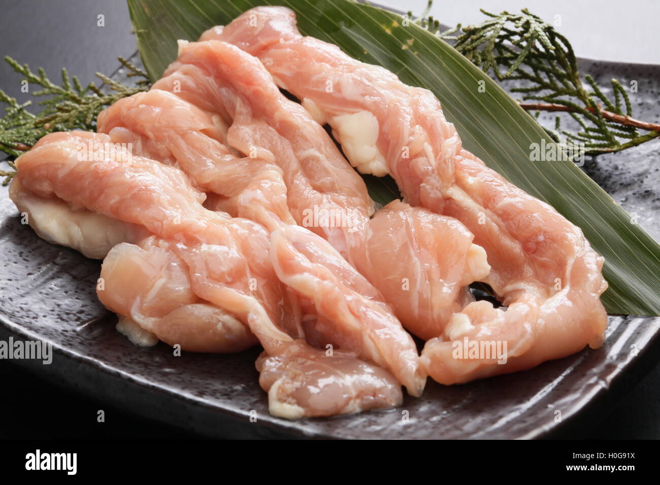 Fresh raw skipper of chicken meat on black platter with green leaf ...