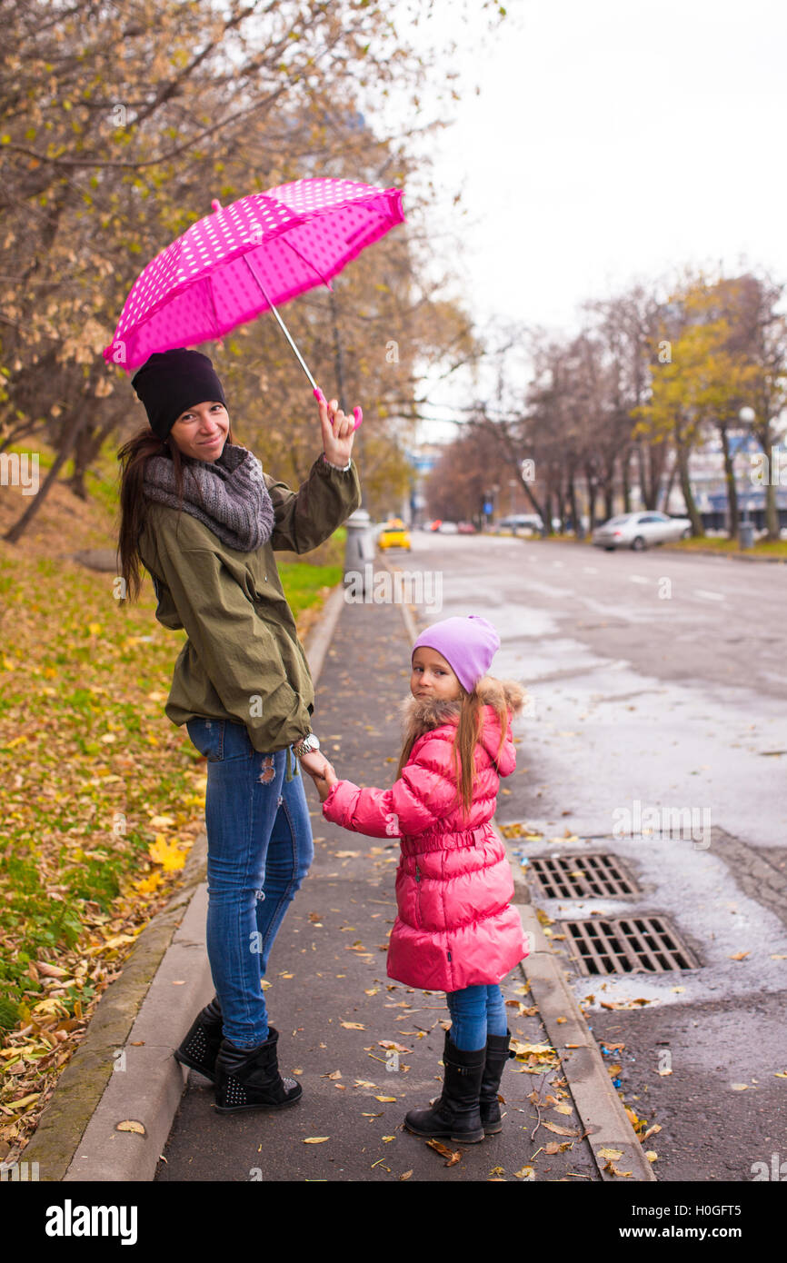 Little girl walking with her mother under an umbrella on a rainy day ...