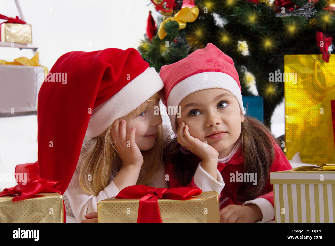 Girls in Santa hats sharing secrets under Christmas tree Stock Photo ...