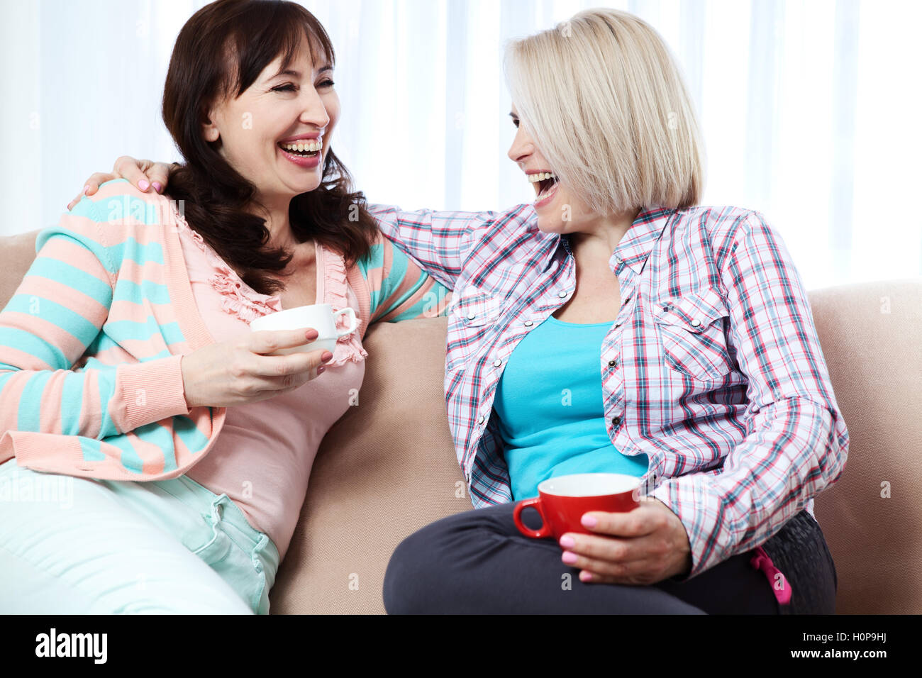 Two happy female friends with coffee cups enjoying a conversation in ...