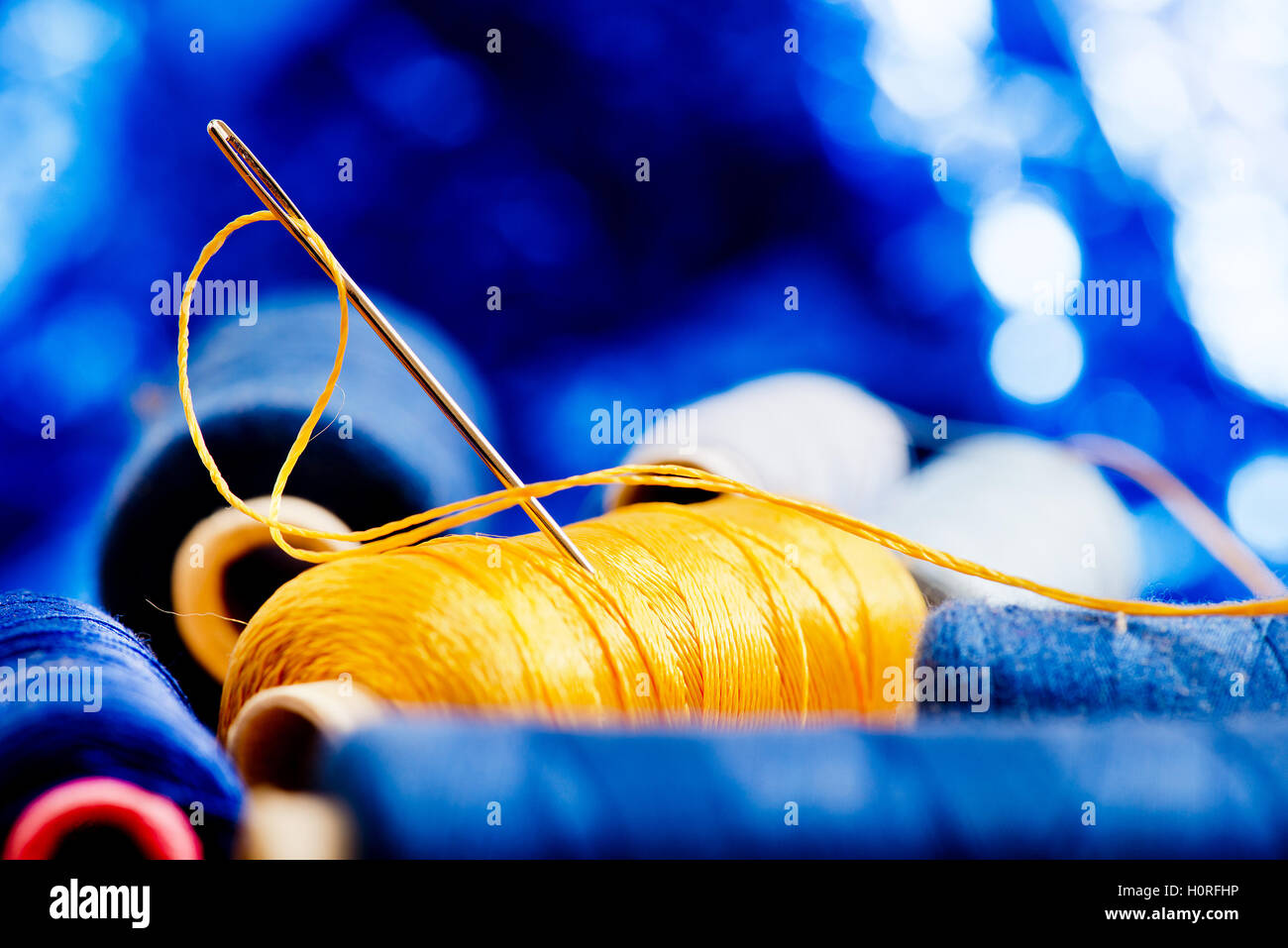 needle and yellow thread on the blue background Stock Photo - Alamy