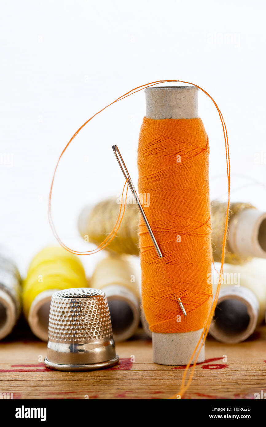 nedle with orange color thread and thimble on the white background ...