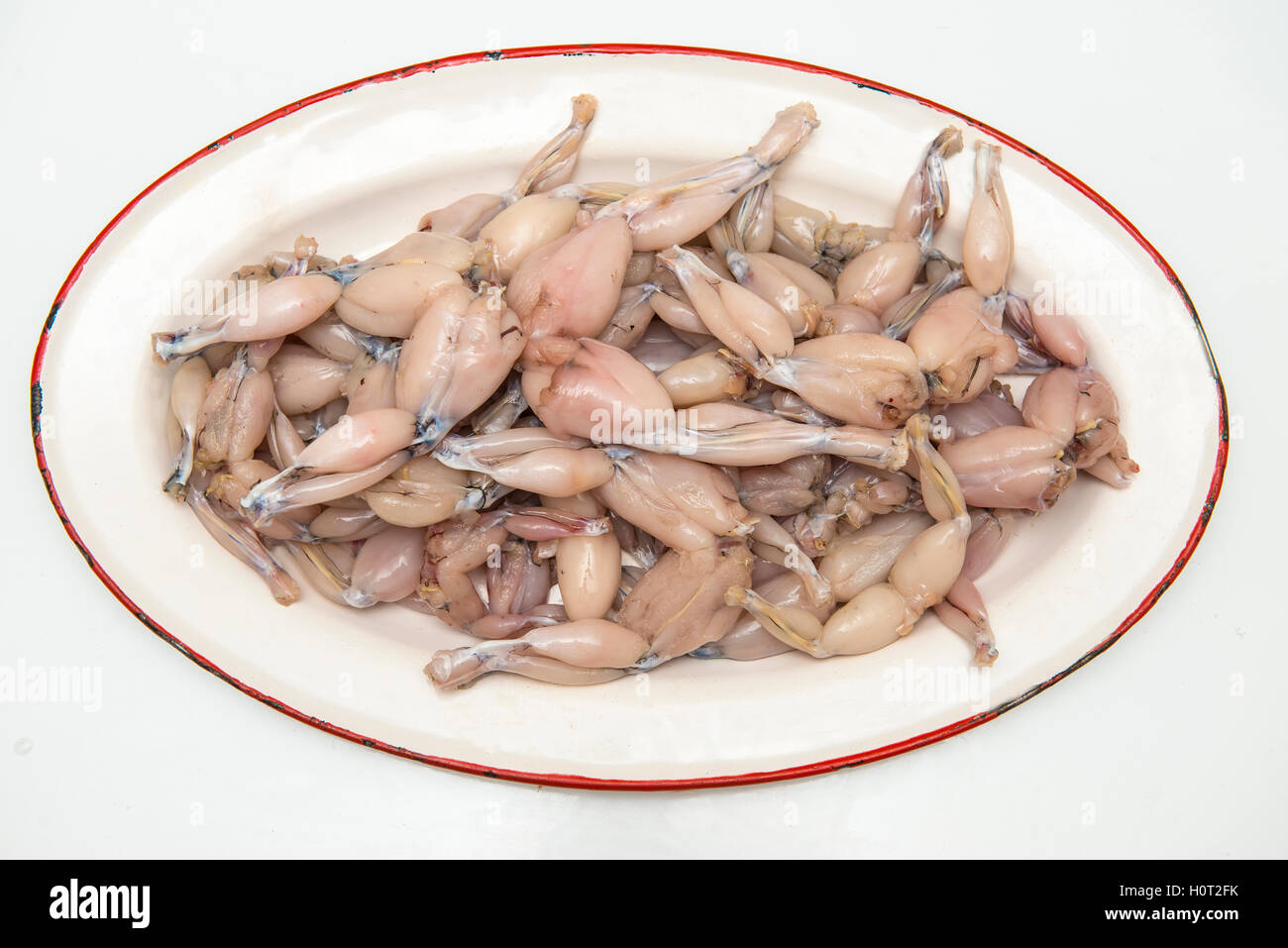 A platter with fresh and raw frog legs ready to be cooked on a white ...