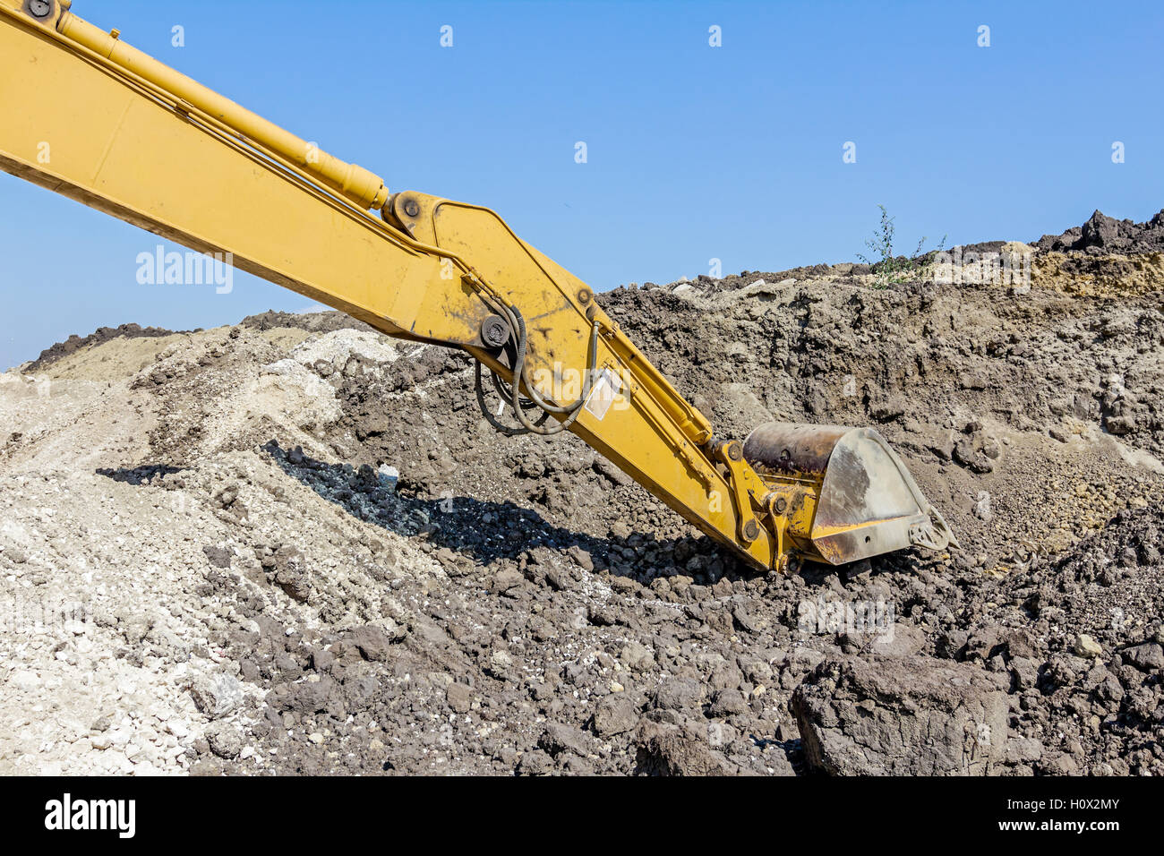 Yellow excavator is digging soil by pulling ground at construction site ...