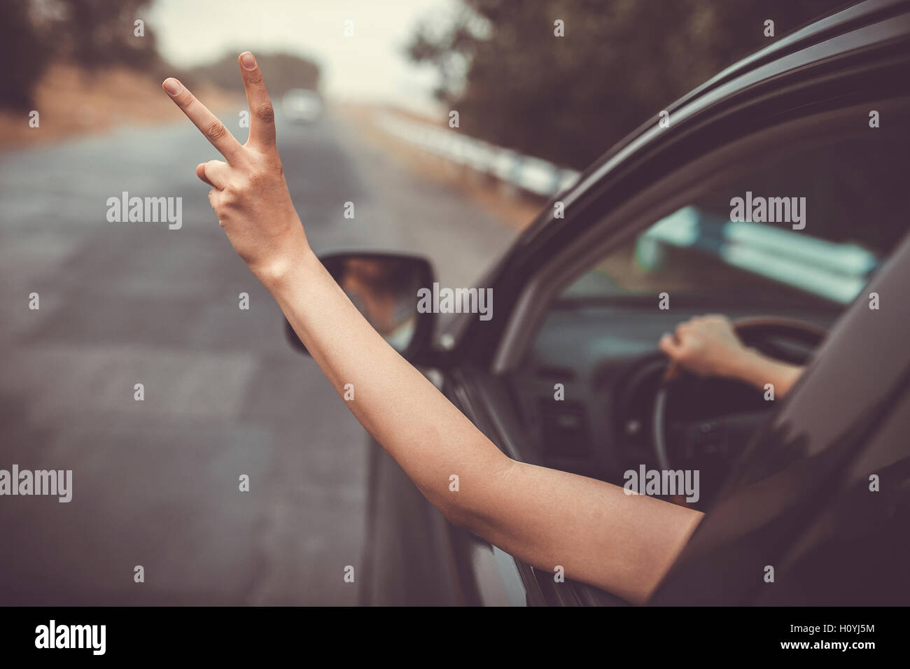 Young happy lady driving a car and making Like / Ok sign with hand out ...
