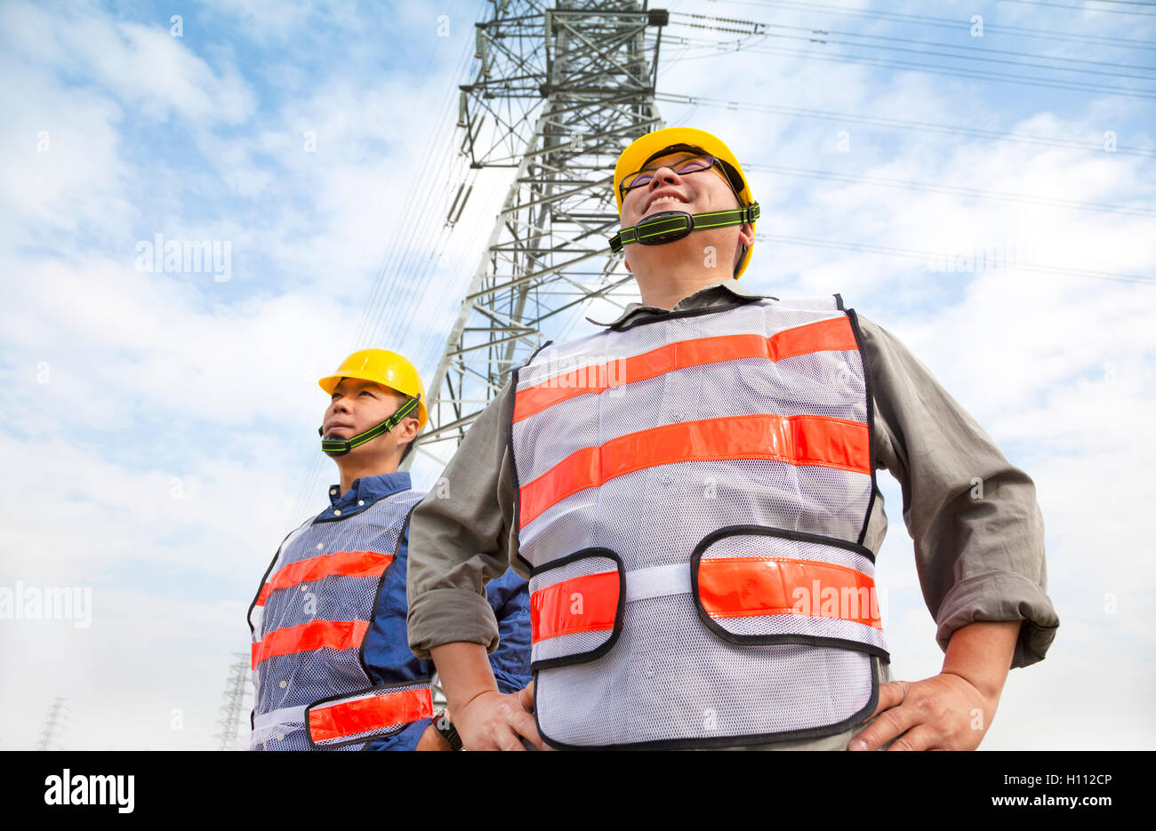 two workers standing before electrical power tower Stock Photo - Alamy