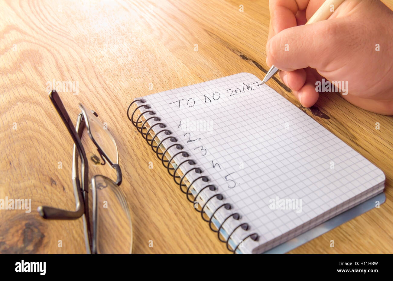 Man's hand writing the to do list for 2017, on a graph spiral notebook ...