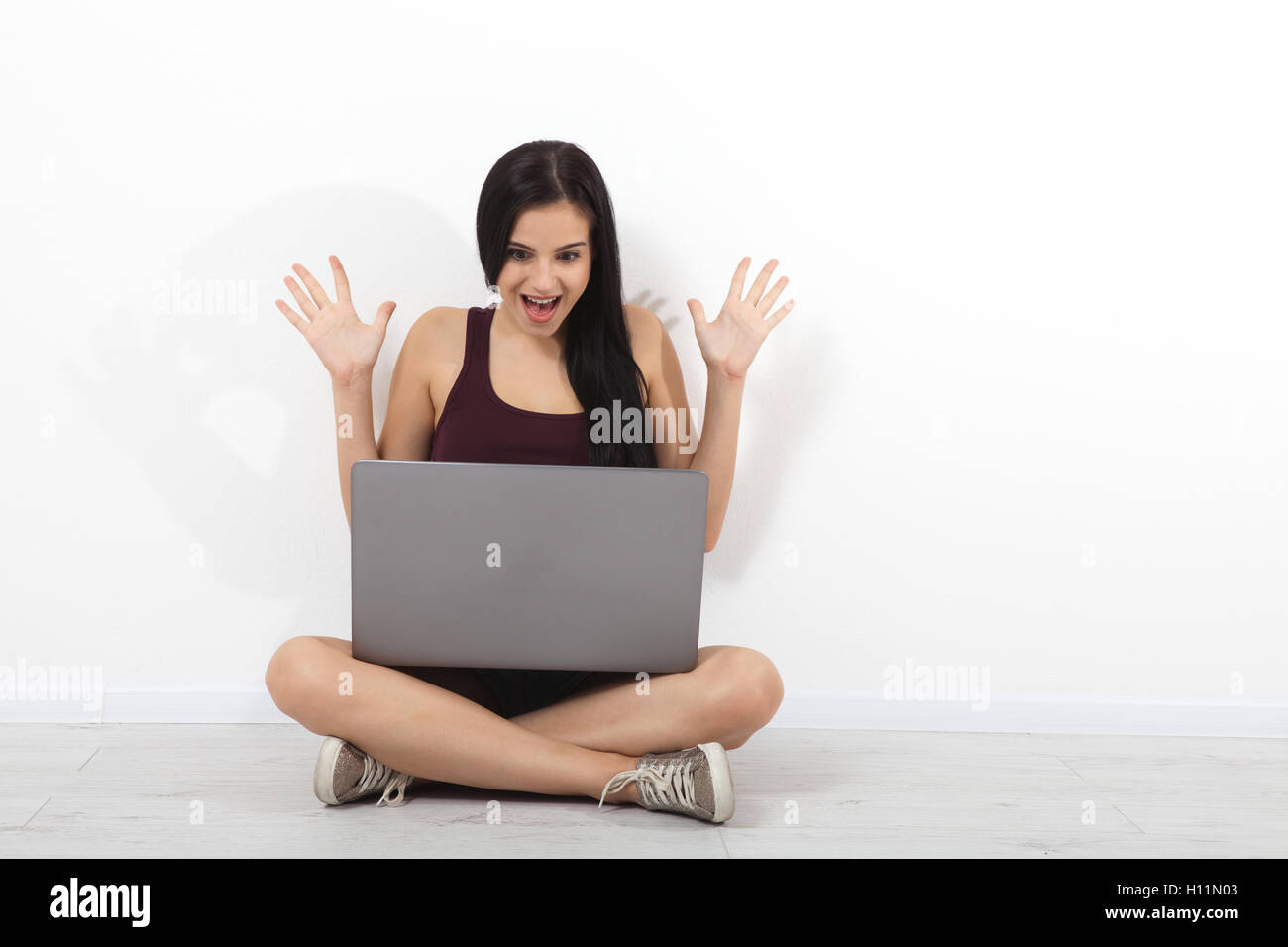 Happy young woman sitting on floor with crossed legs and using laptop ...