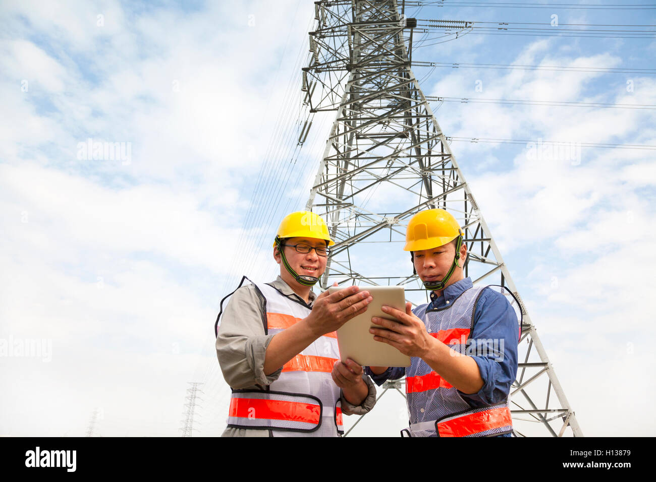 two workers standing before electrical power tower Stock Photo - Alamy