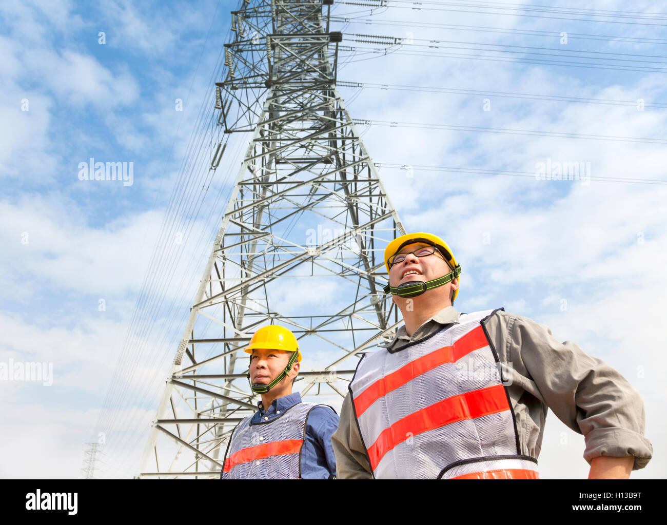 two workers standing before electrical power tower Stock Photo - Alamy