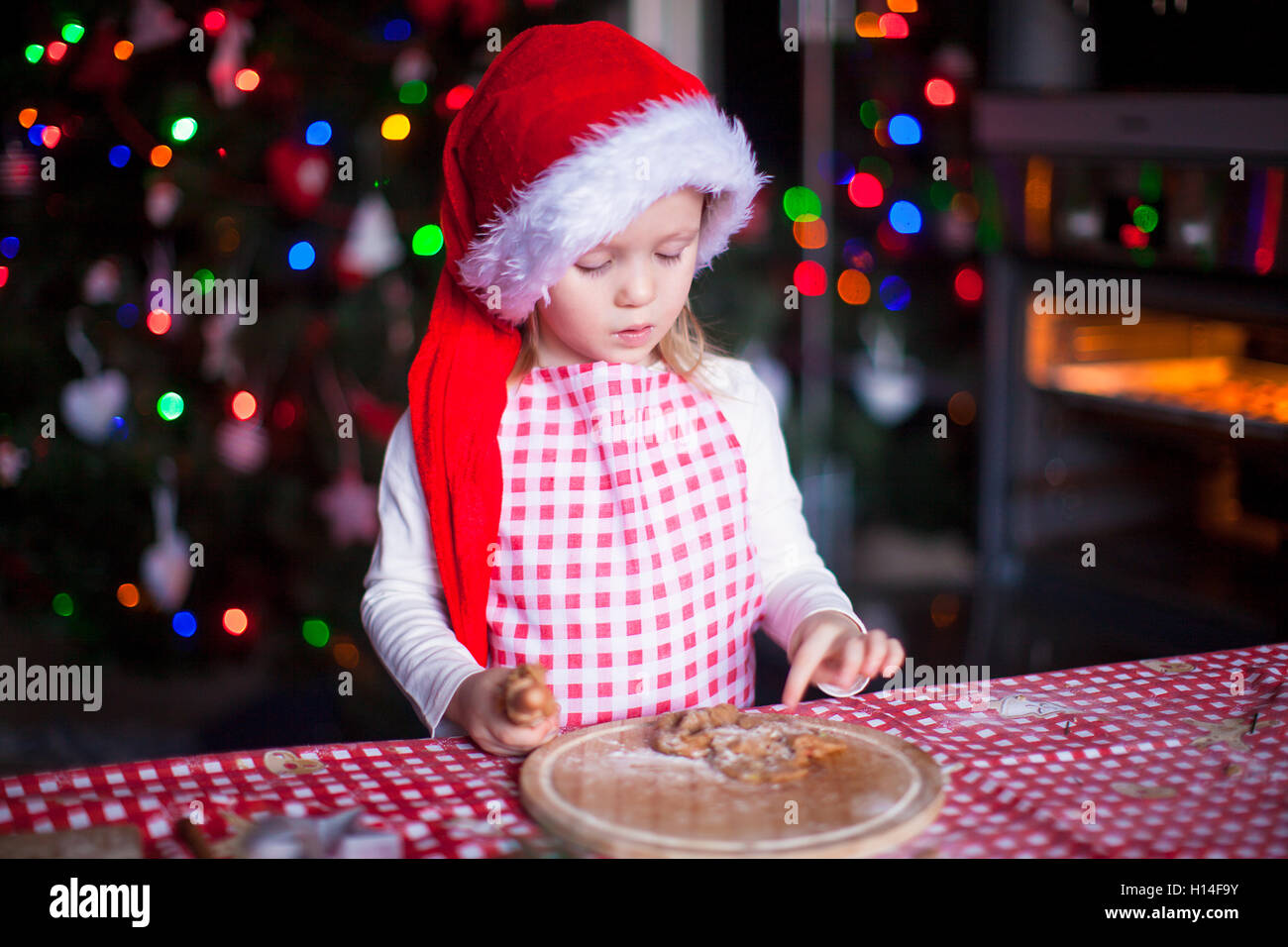 Adorable little girl eating the dough for ginger cookies in kitchen ...