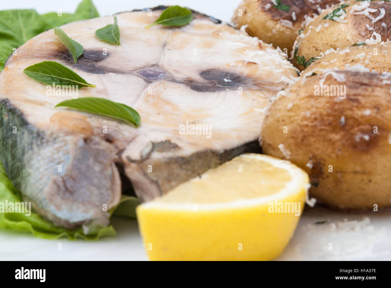 Fried red tuna steak served with piece of lemon and baked potato on the ...