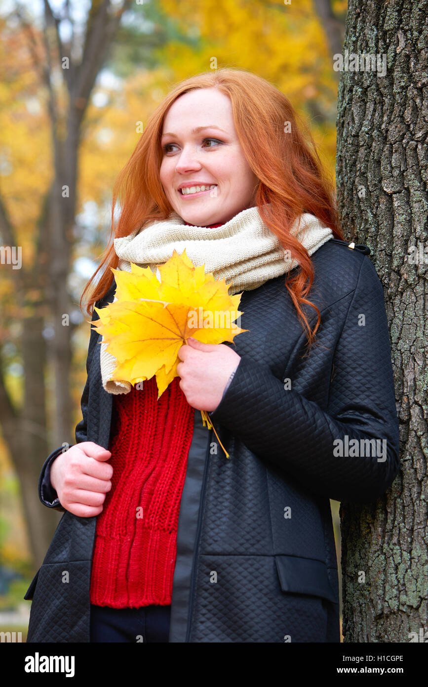 girl portrait with yellow leaf in hand in autumn forest, stand near big ...