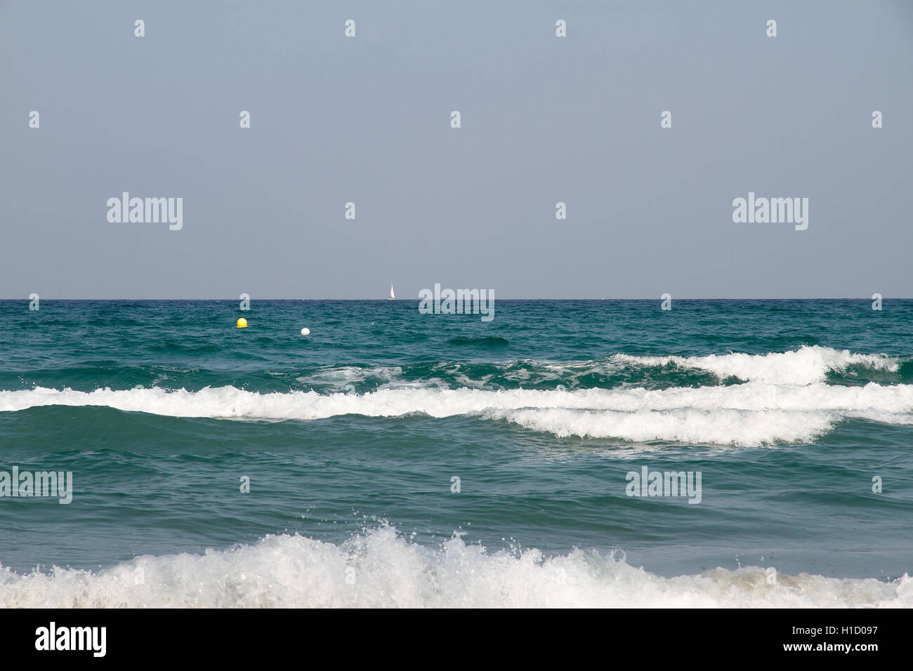 view of the sea with waves in the foreground and a sailboat in the ...