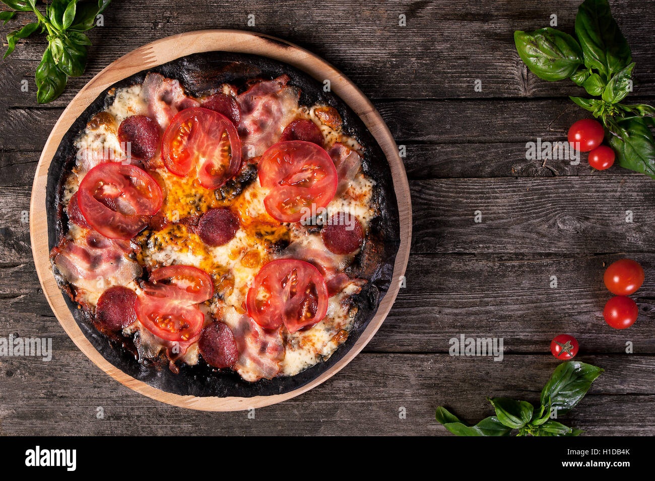 Black pizza with salami, ham, tomato and cheese. Base with cuttlefish ...