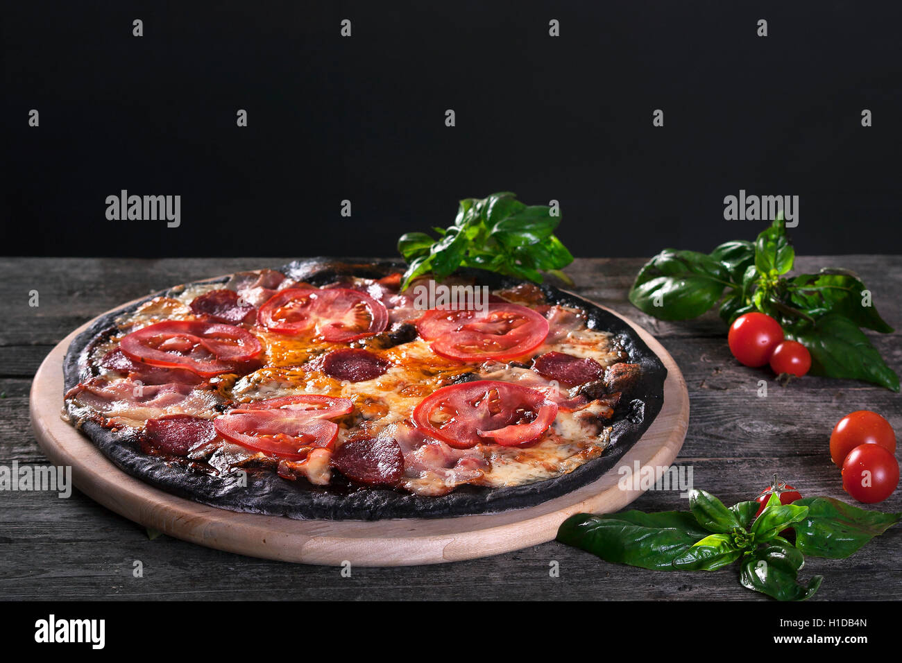 Black pizza with salami, ham, tomato and cheese. Base with cuttlefish ...