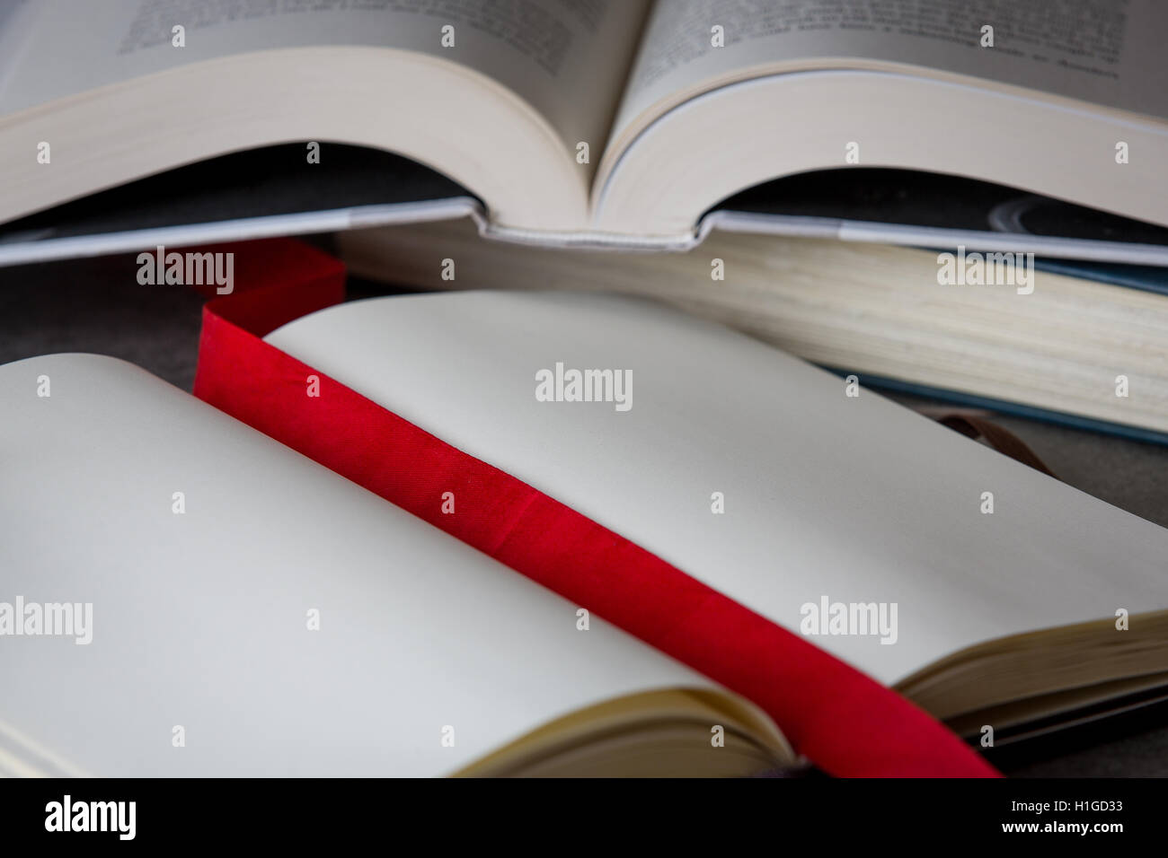 Multiple open books on table, one marked with a red ribbon Stock Photo ...