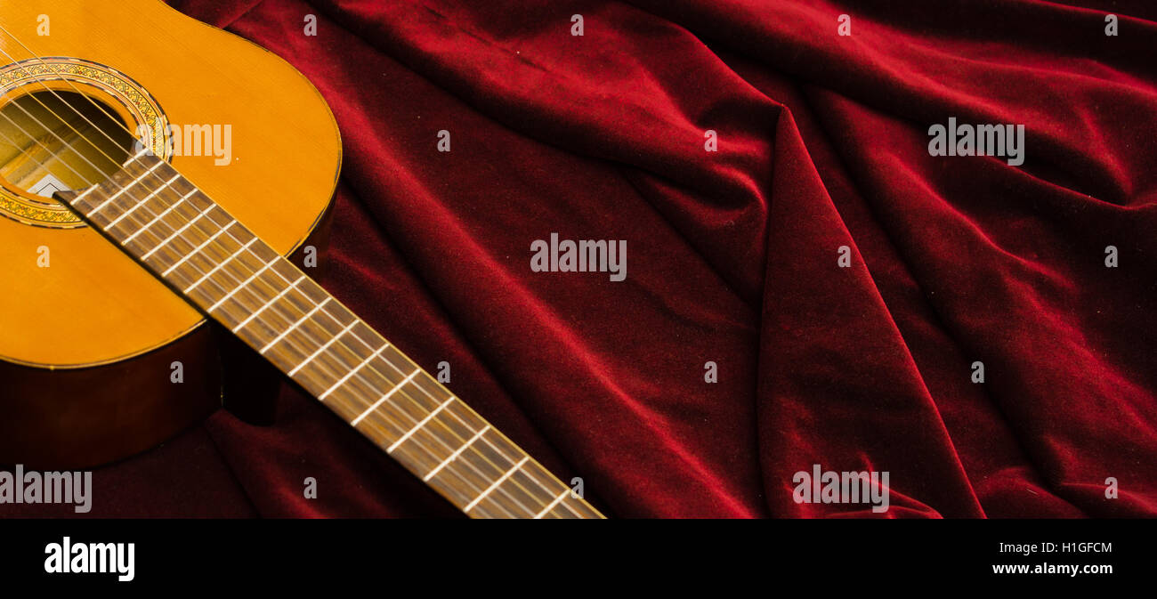 Classical nylon guitar lying on red velvet textile, artistic instrument ...