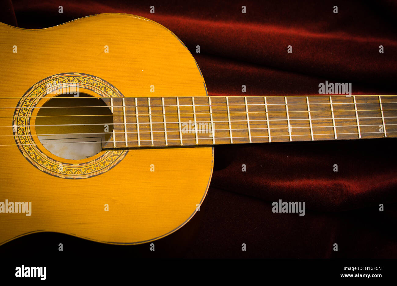 Classical nylon guitar lying on red velvet textile, artistic instrument ...