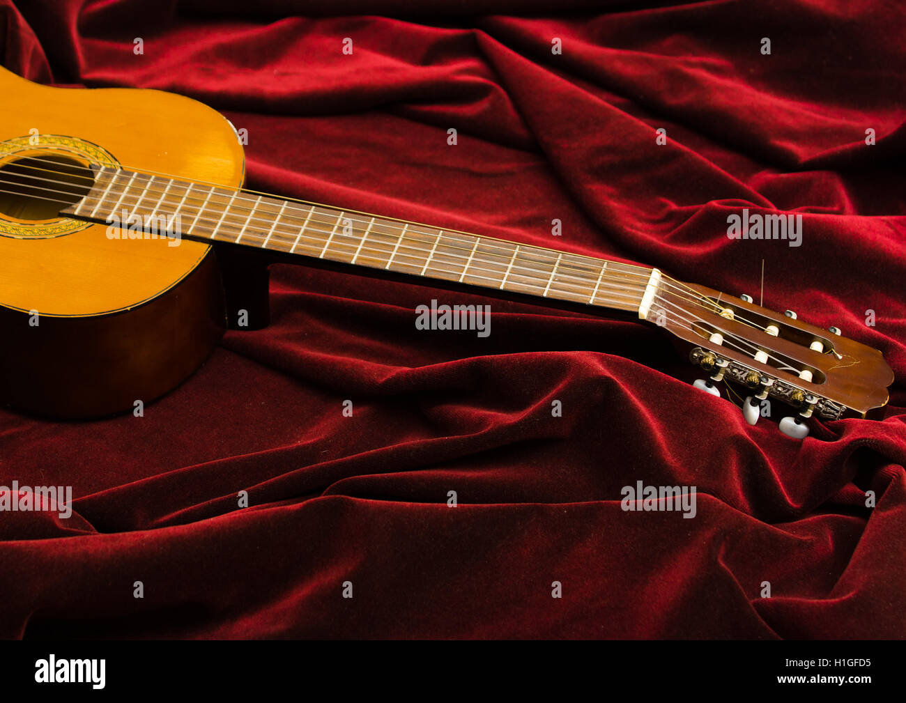 Classical nylon guitar lying on red velvet textile, artistic instrument ...