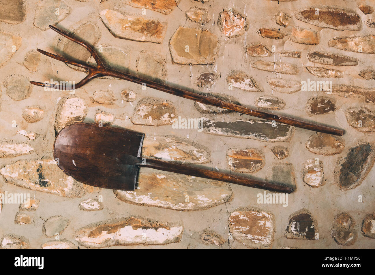 Traditional wooden pitchfork and shovel on a stone wall background ...