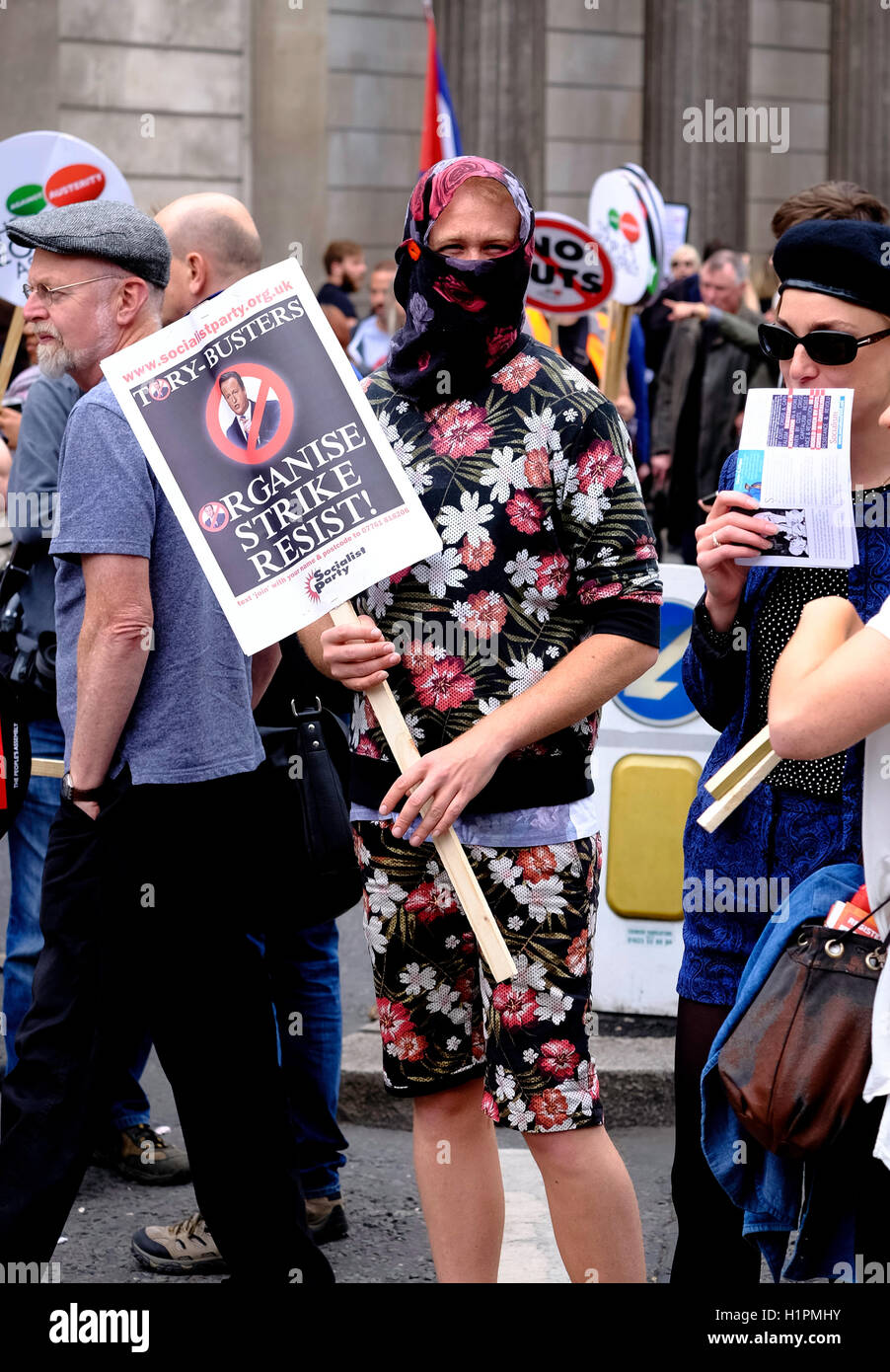 A male protester with his face hidden stands holding a placard and ...
