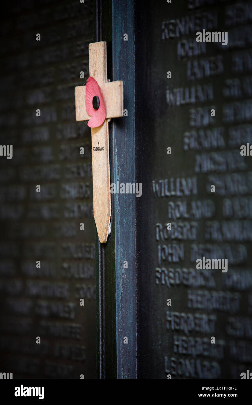 A wooden remembrance cross with poppy on a war memorial with names of ...