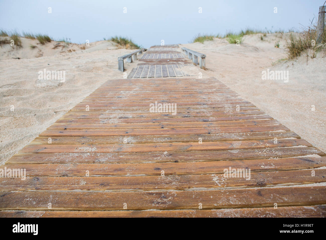 A wooden walk way or boardwalk crossing the low sand dunes to a sandy ...