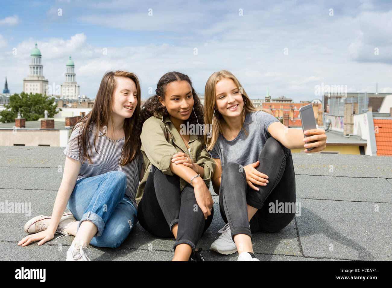 Germany Berlin Three Teenage Girls Sitting On Roof Top Taking Selfie