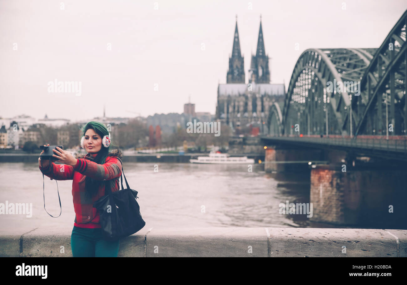 Germany, Cologne, woman with ear muff taking selfie with polaroid ...